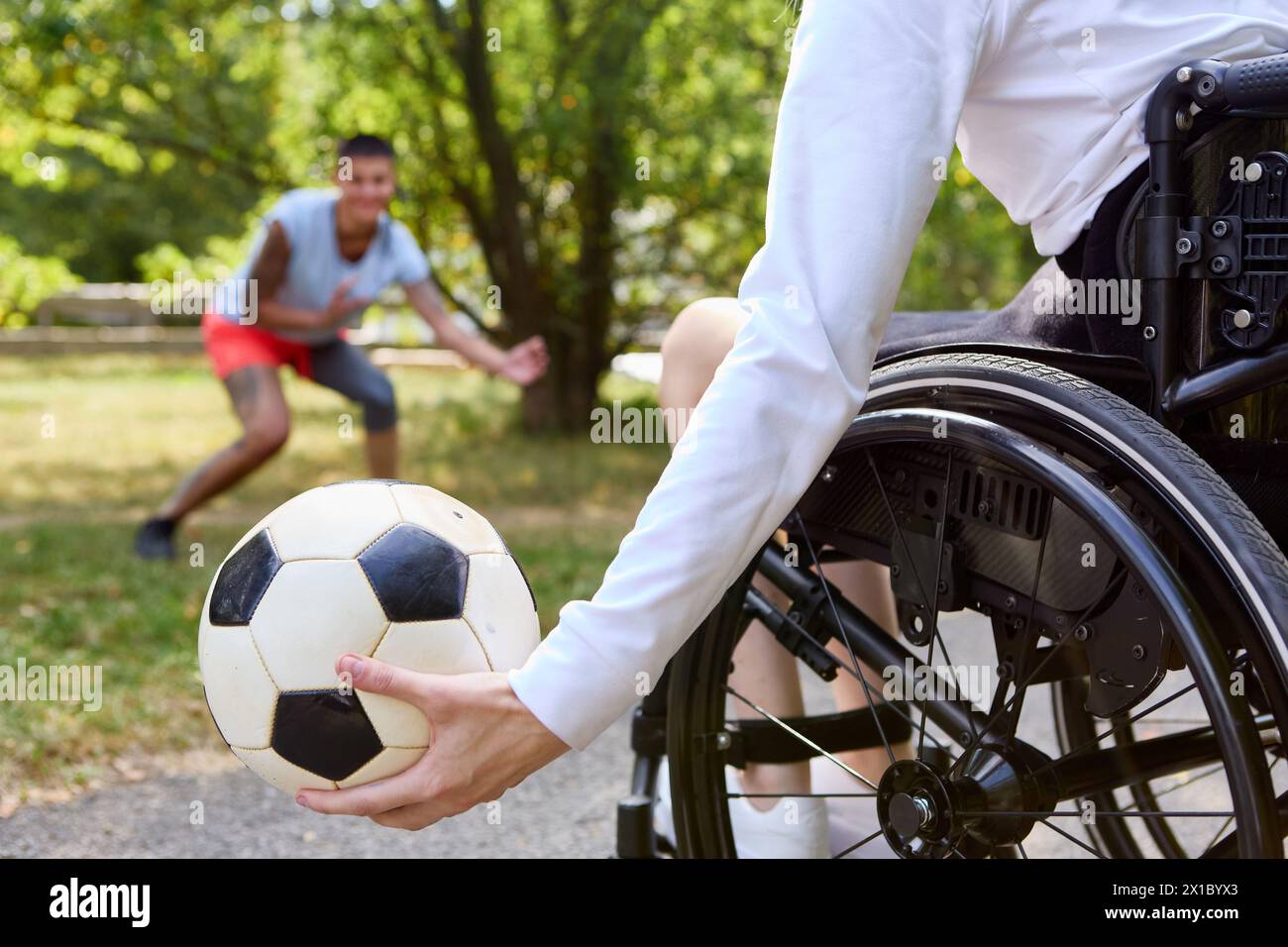 A person using a wheelchair engaging in an active soccer game with a friend outdoors, depicting ...