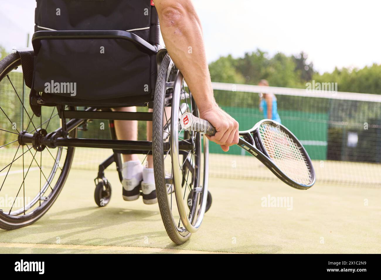 A person in a wheelchair holds a tennis racket on a sunny court ...