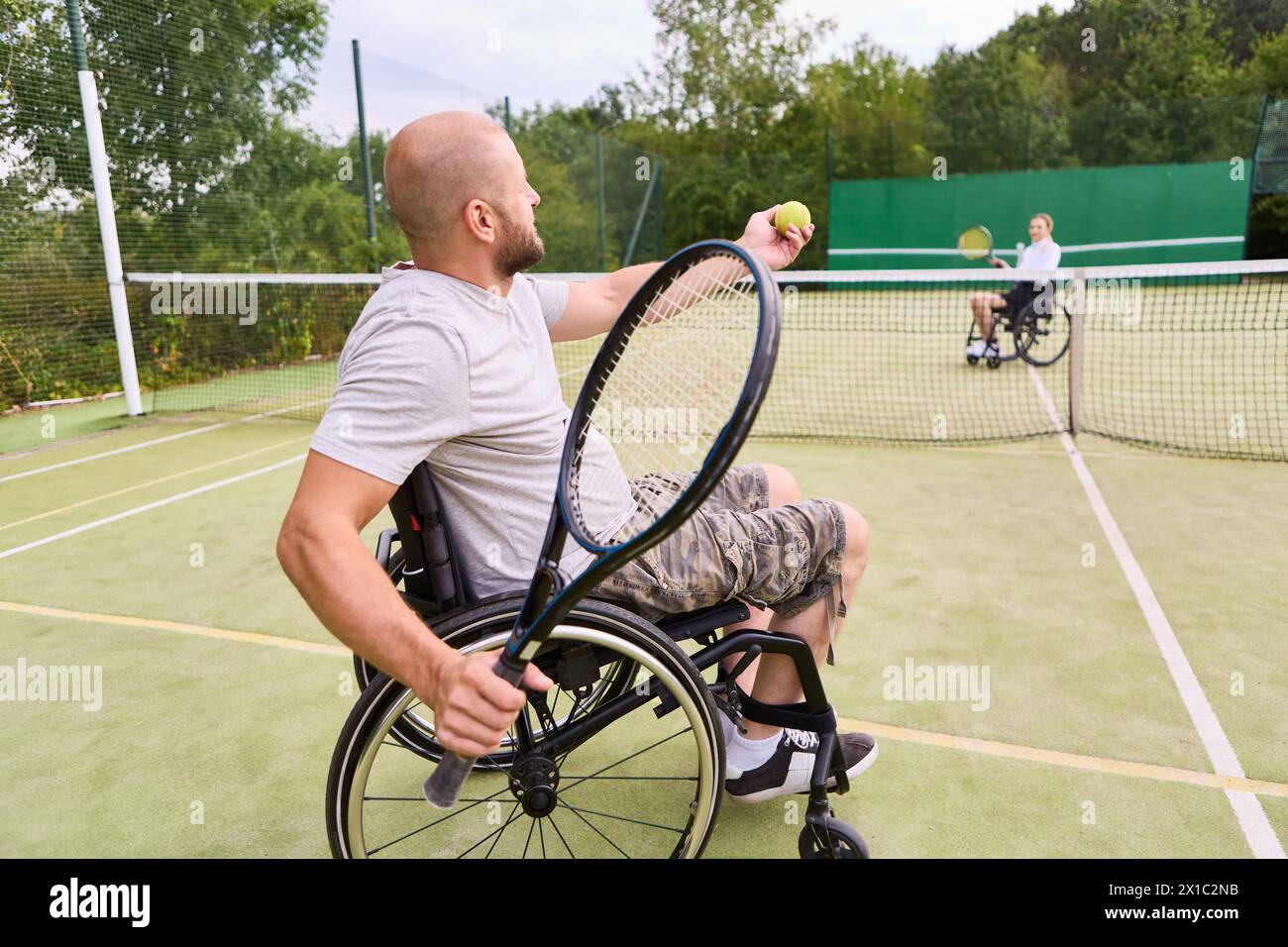 Two people who use wheelchairs are engaged in a friendly tennis match ...