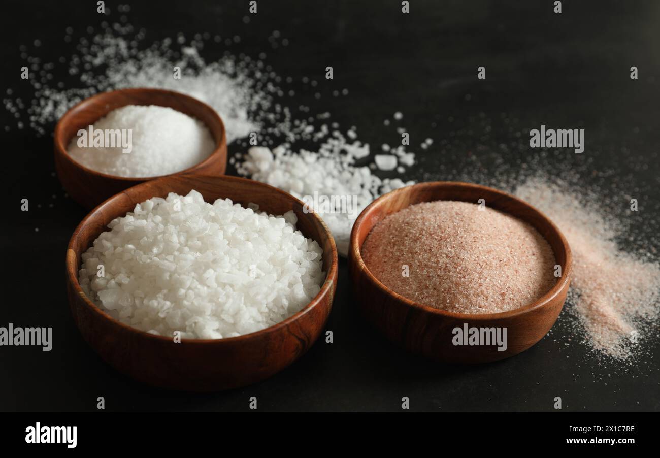 Different types of organic salt in bowls on black table, closeup Stock ...