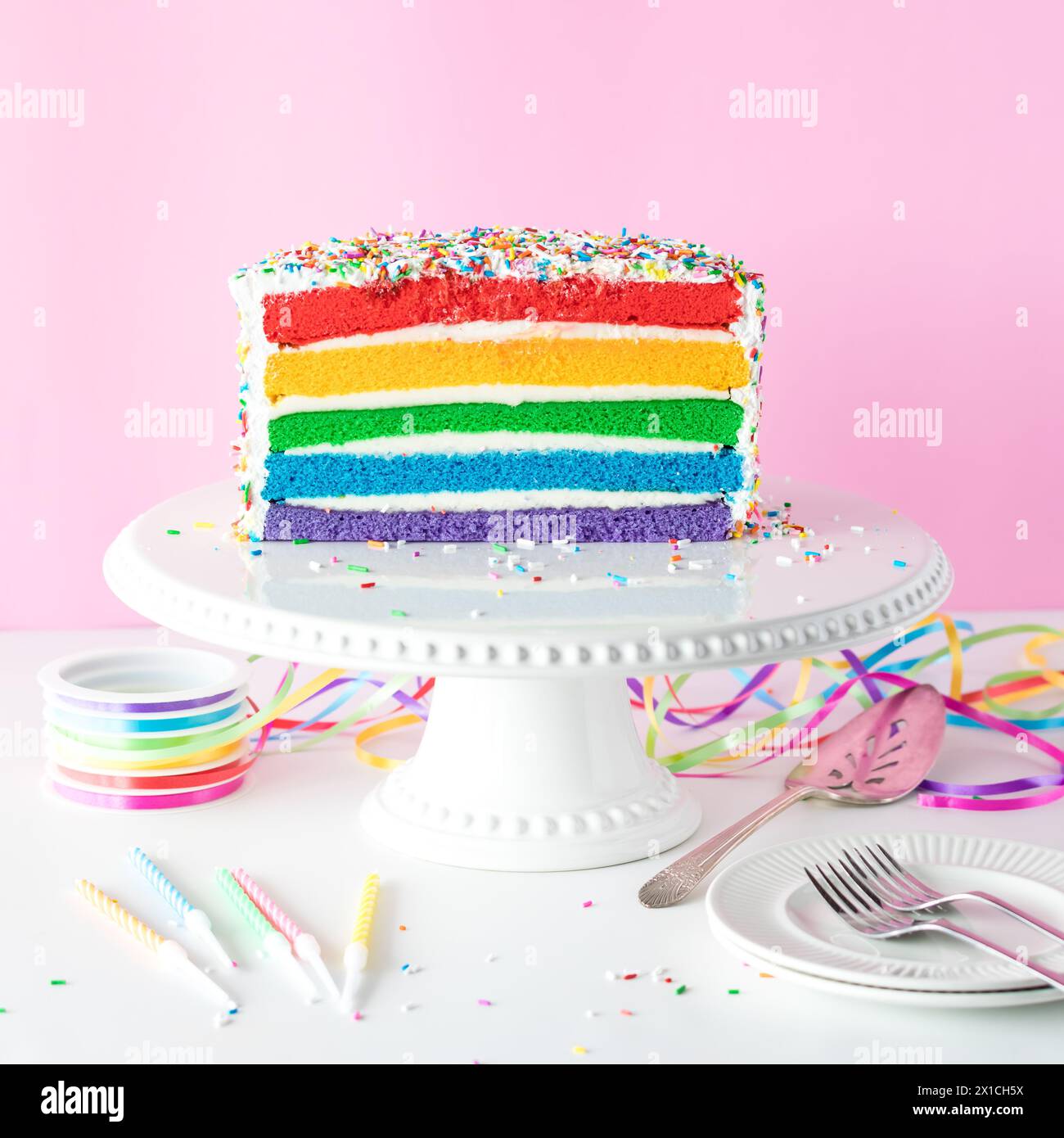 A bright rainbow layered birthday cake surrounded by colourful ...