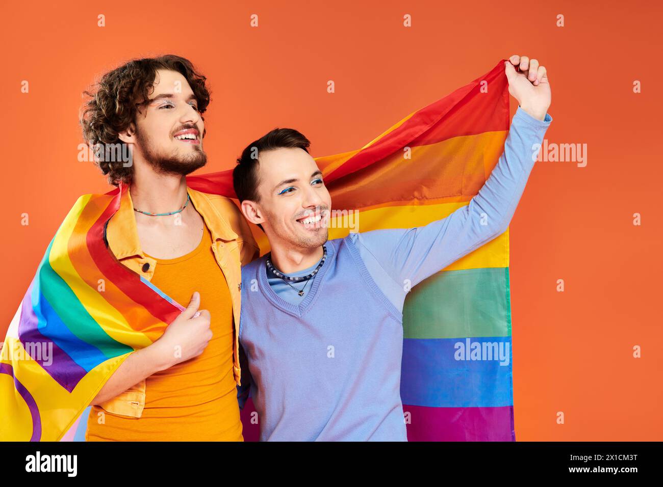 cheerful appealing young gay men in cozy attires with rainbow flag on ...