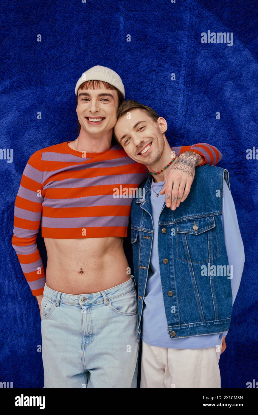 two positive good looking gay men in vibrant clothes posing on dark ...