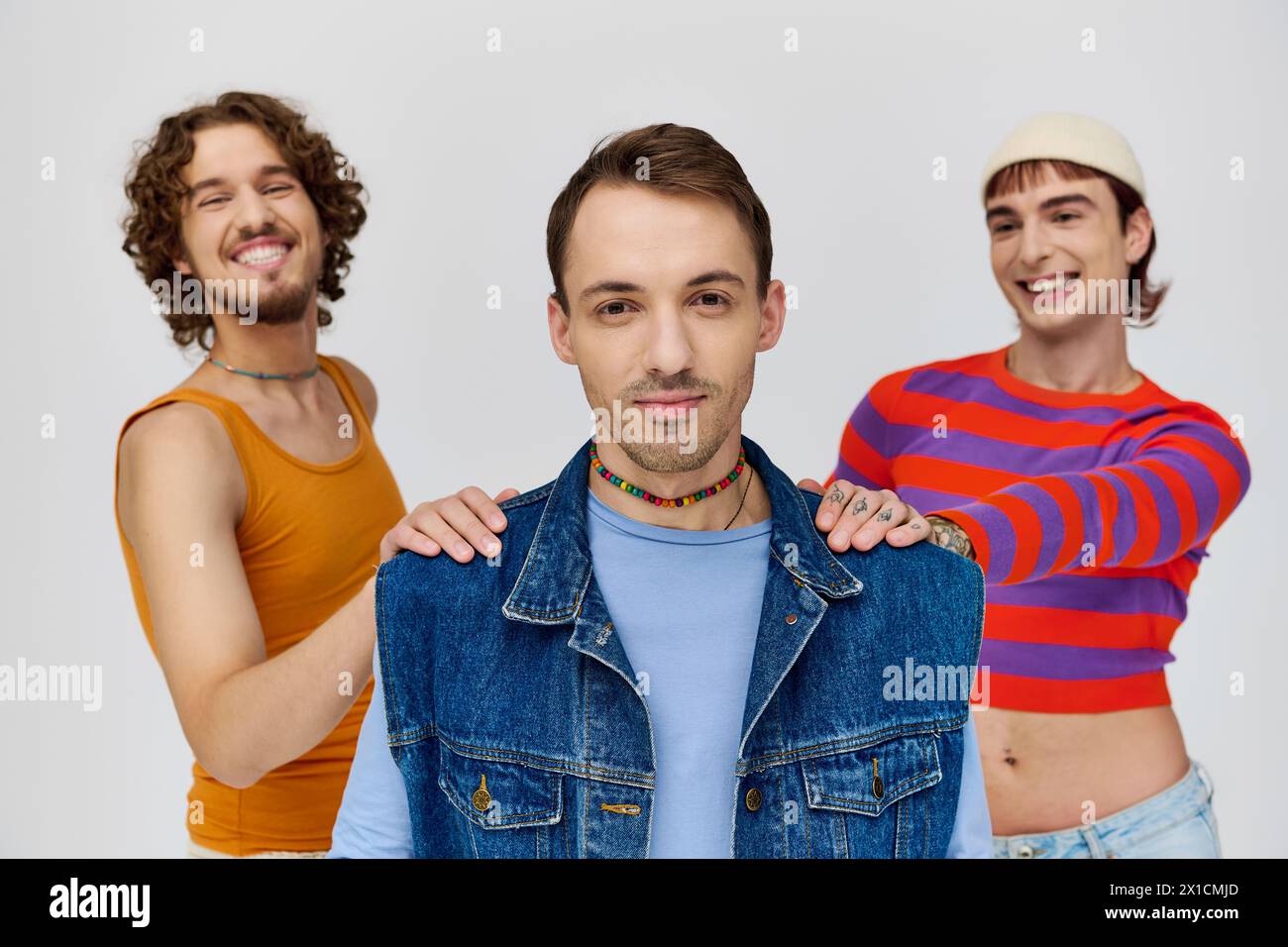 merry handsome gay men in vibrant attires posing together on gray ...