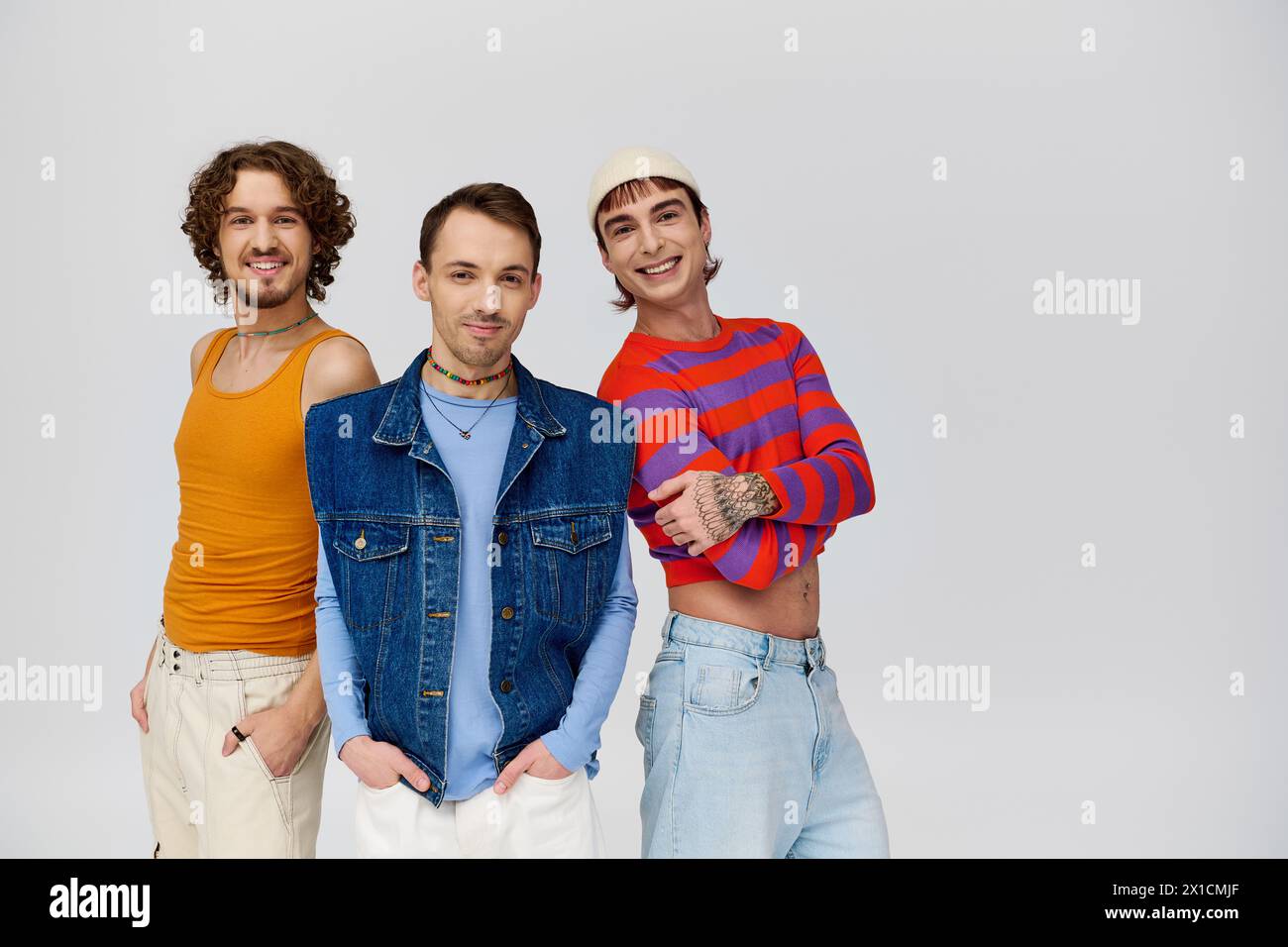 joyous handsome gay men in vibrant attires posing together on gray ...