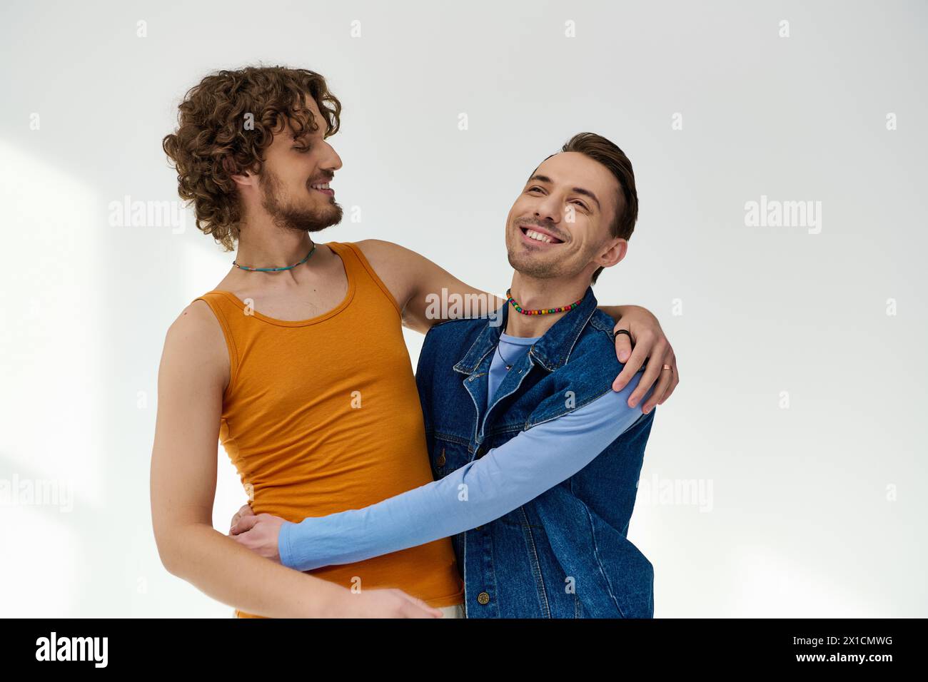 good looking cheerfull lgbtq friends in vibrant clothes hugging on gray ...