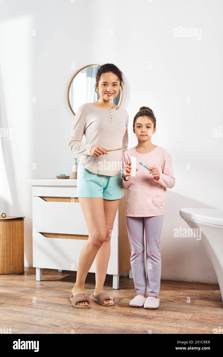 A brunette woman stands with her preteen daughter in a modern bathroom ...