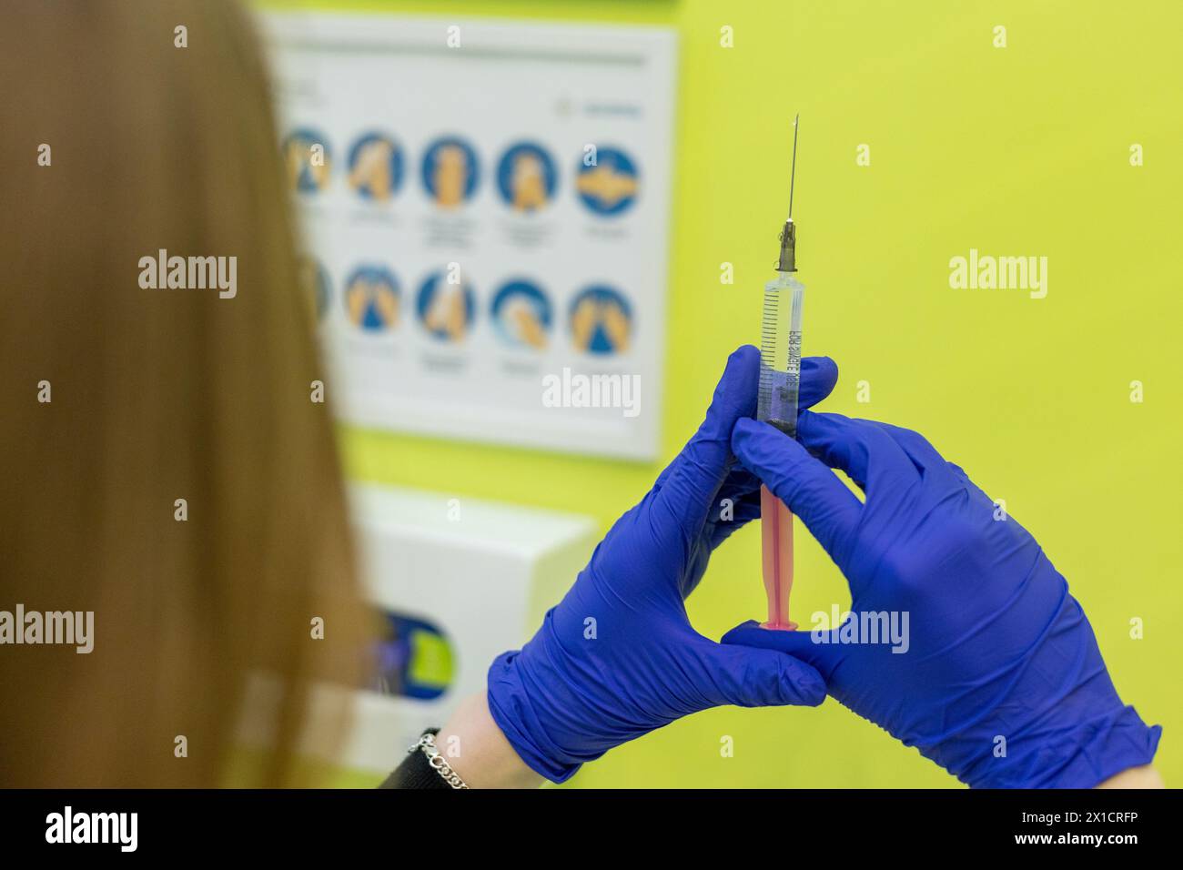 A nurse in blue gloves draws medicine into a syringe for an injection ...