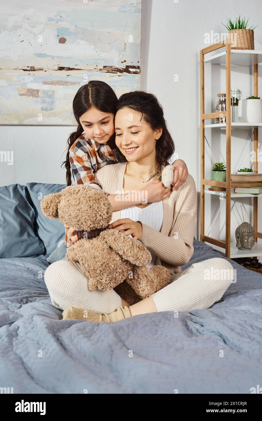A mother and daughter sitting on a bed, hugging a teddy bear in a heartwarming embrace, enjoying ...