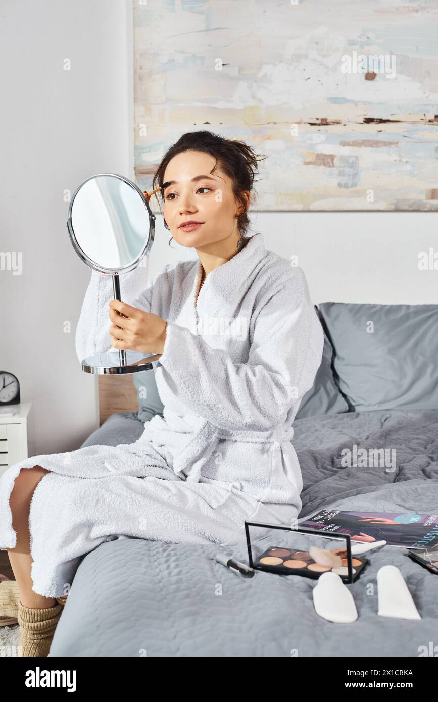 A brunette woman in a white bathrobe sits on a bed, carefully examining ...