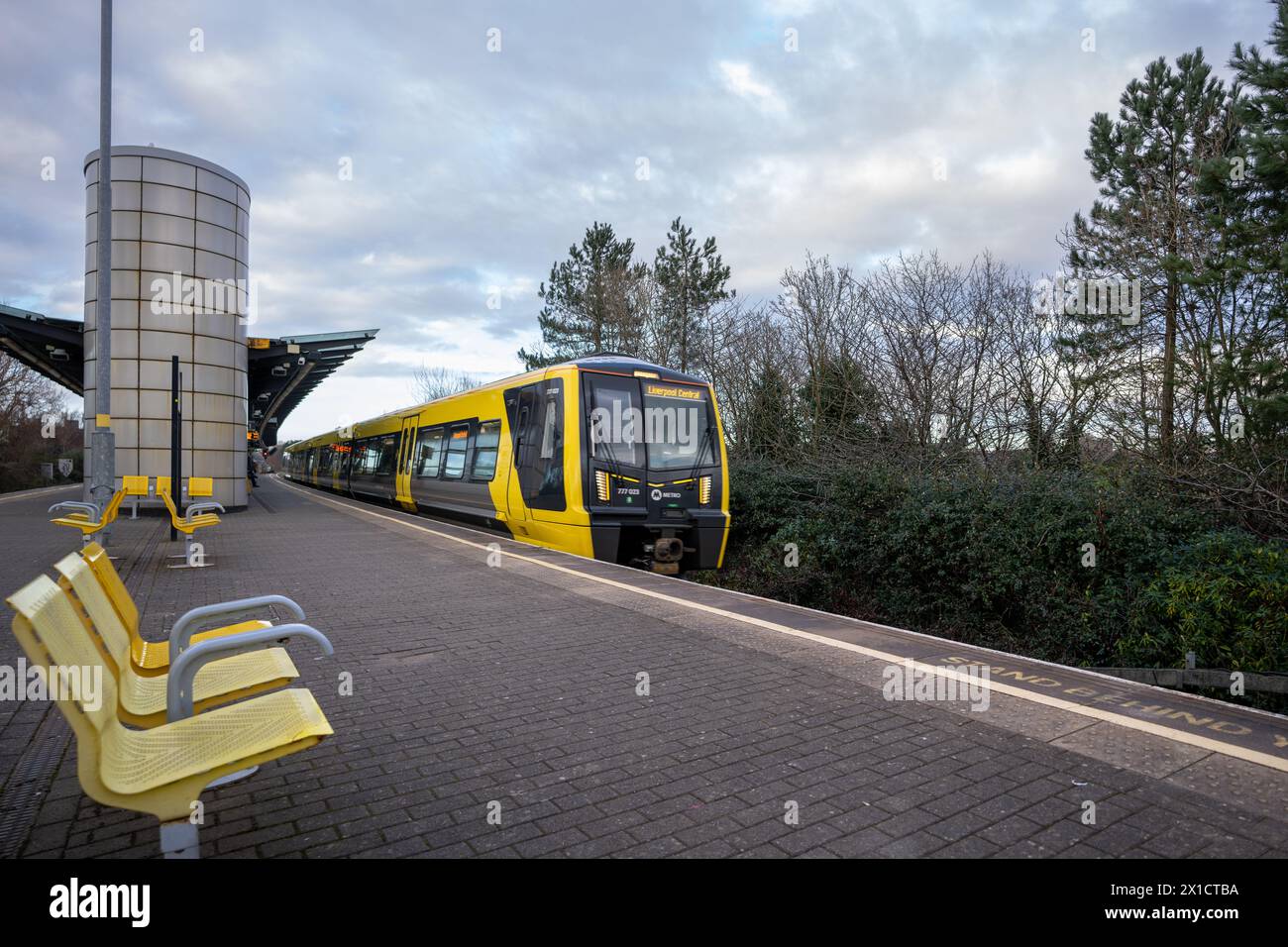 Merseyrail train arriving at platform with yellow seats in foreground ...