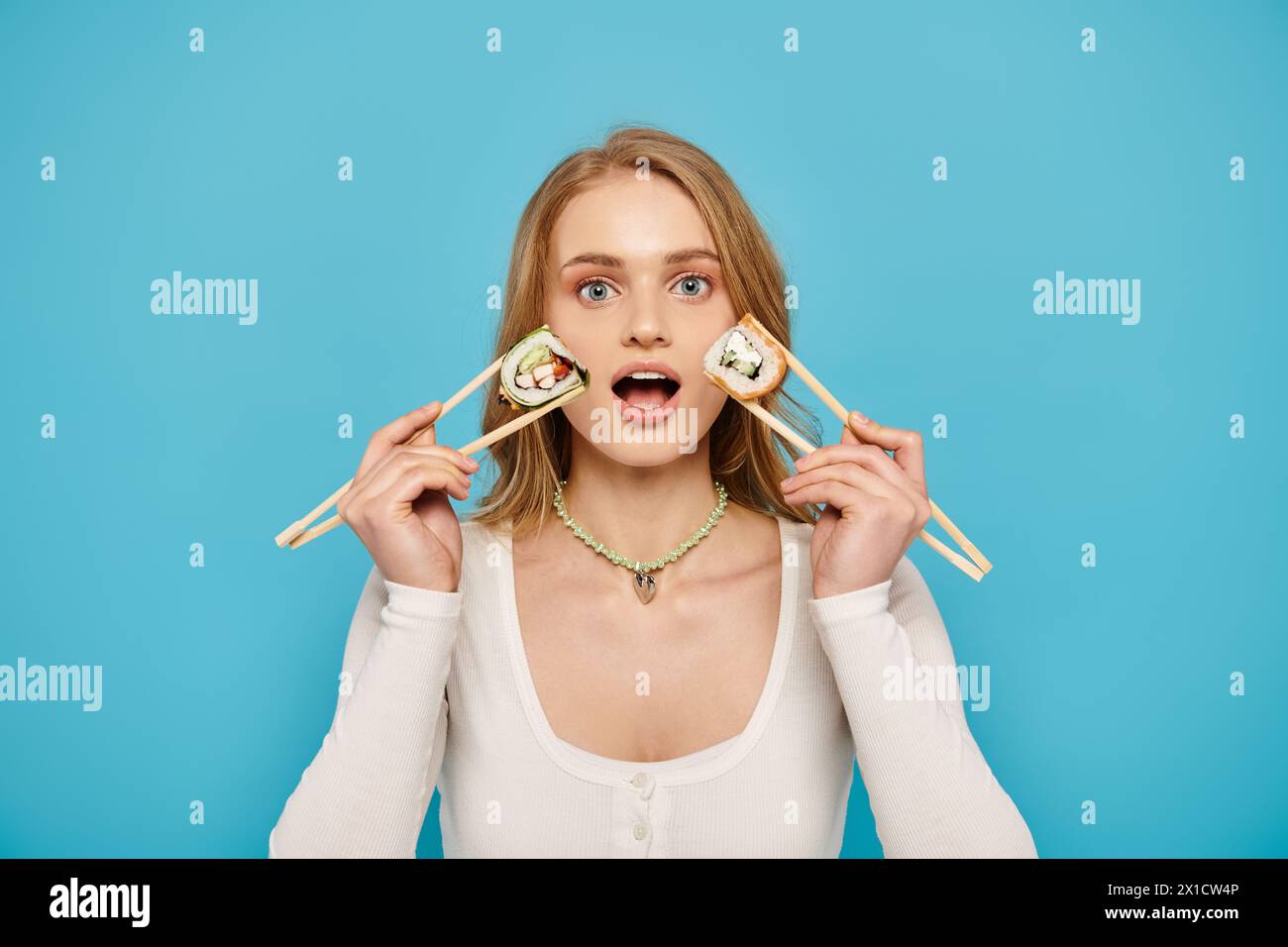 A beautiful woman with blonde hair holding two chopsticks over her eyes ...