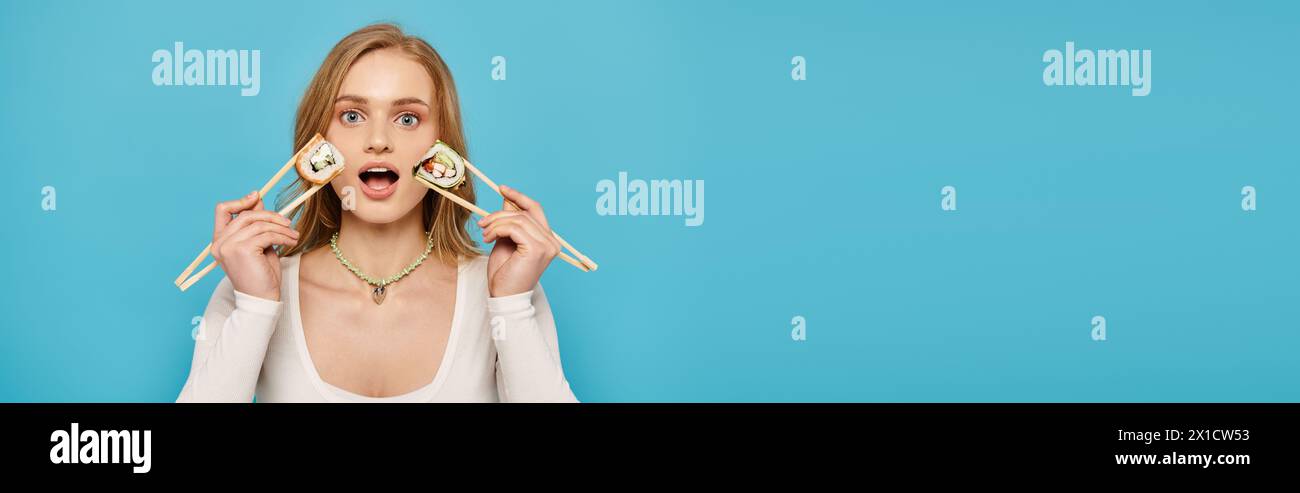 A beautiful woman with blonde hair holds up chopsticks with sushi near ...