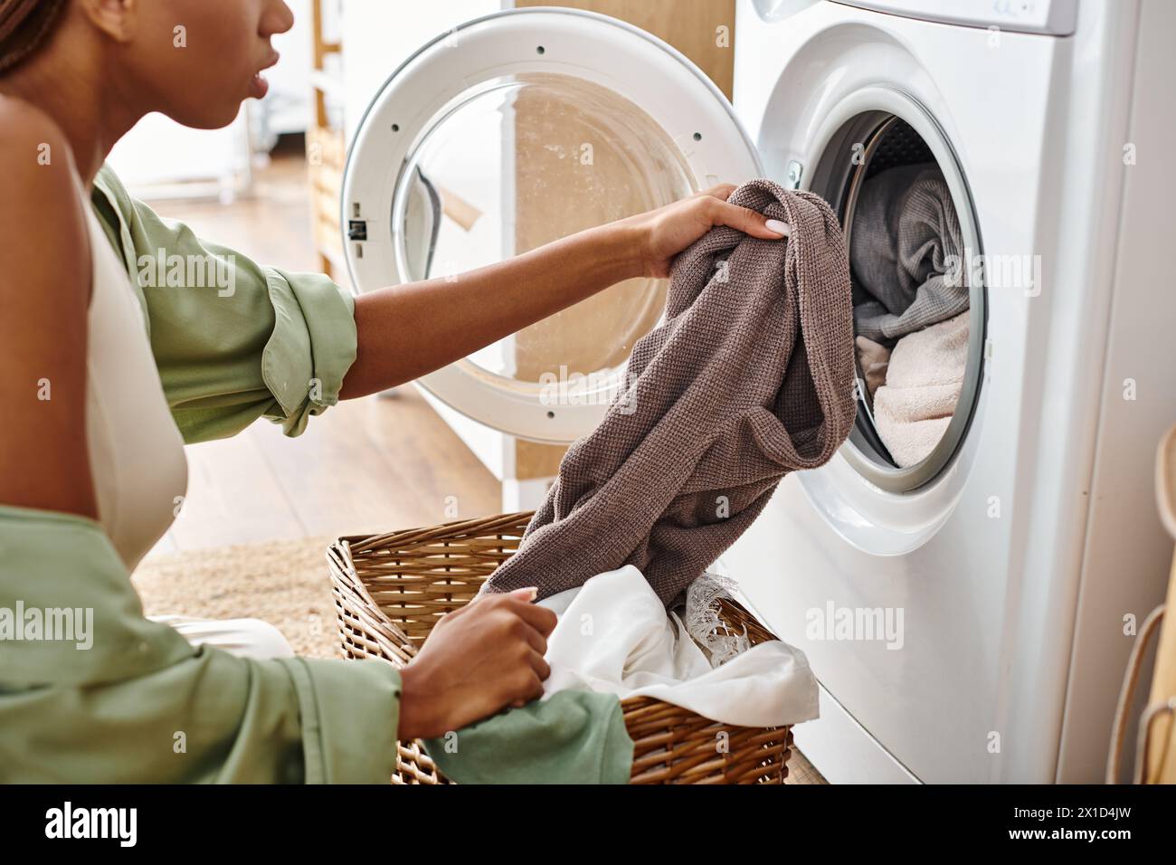 African American woman with afro braids putting a cloth into a dryer in a bathroom during ...