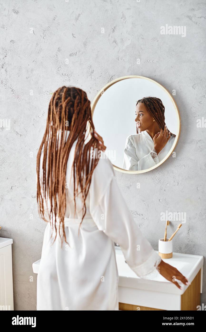 A woman with dreadlocks stands in front of a mirror in a modern ...
