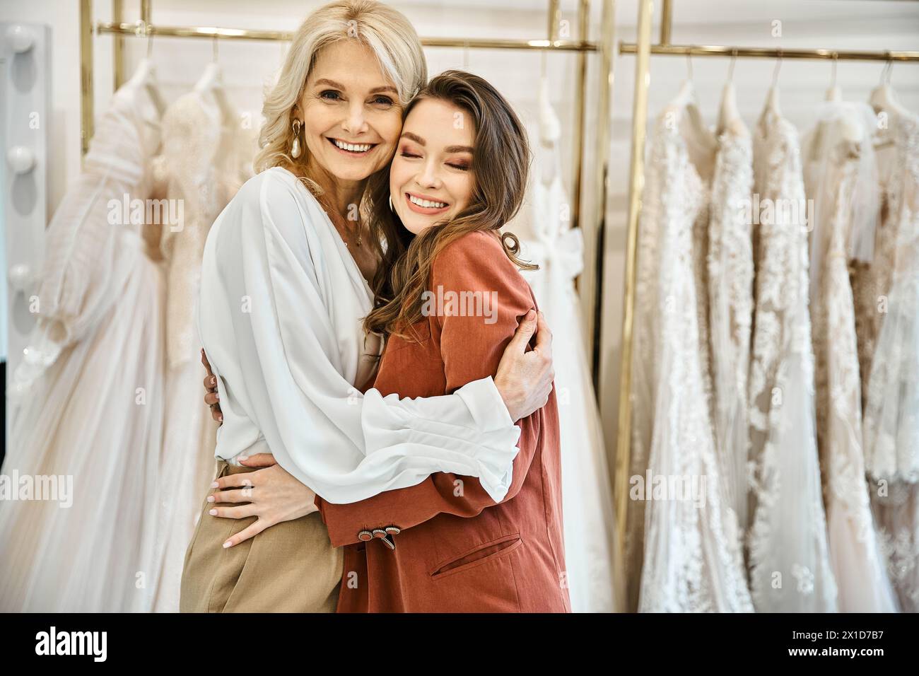 Two women hug in front of wedding dresses, a young bride and her mother ...