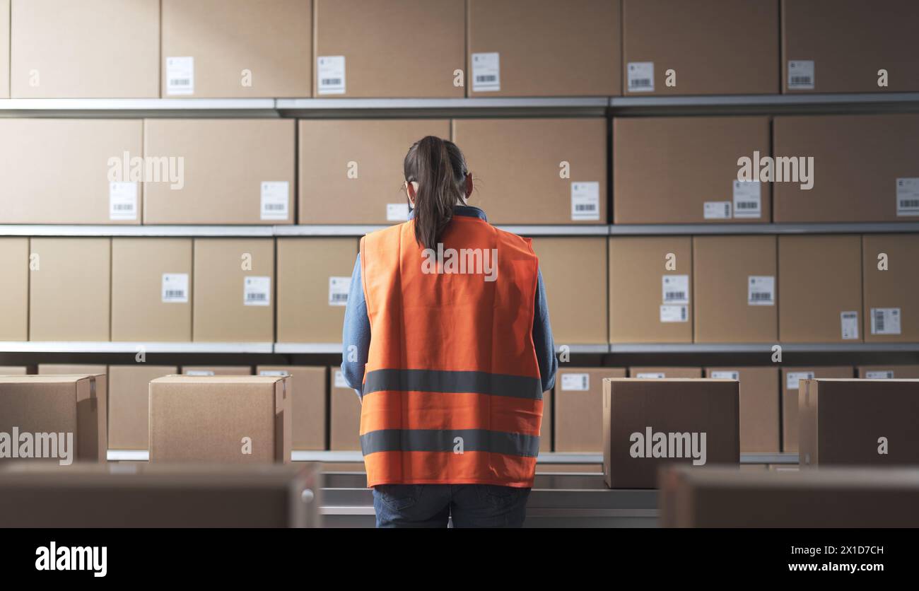 Female warehouse worker checking boxes on the conveyor belt, back view ...