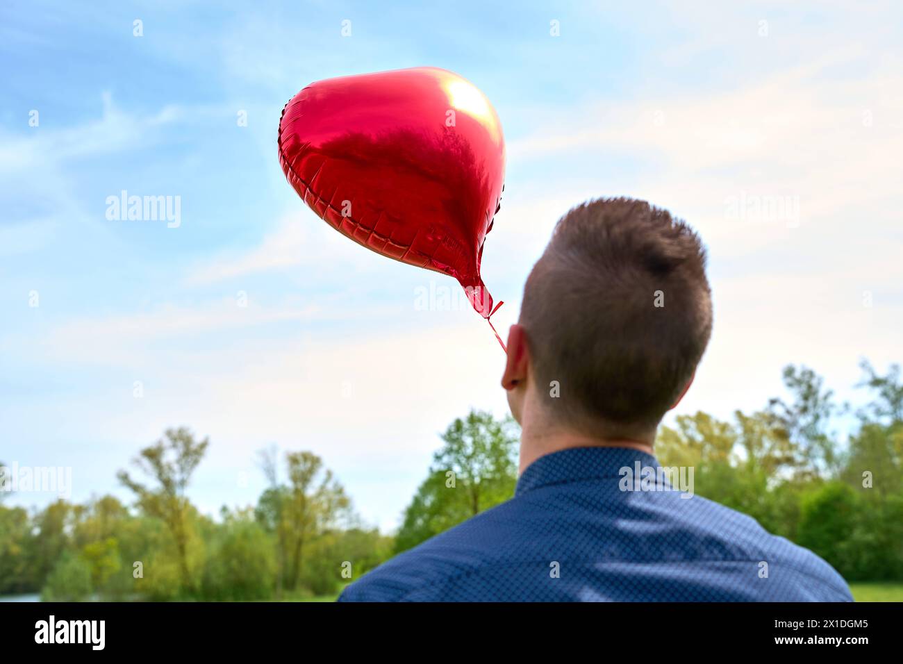 14 April 2024: Young man holding a red helium balloon in the shape of a ...