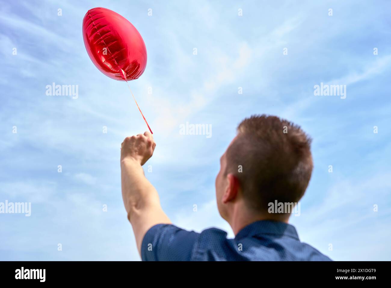 14 April 2024: Young man holding a red helium balloon in the shape of a ...