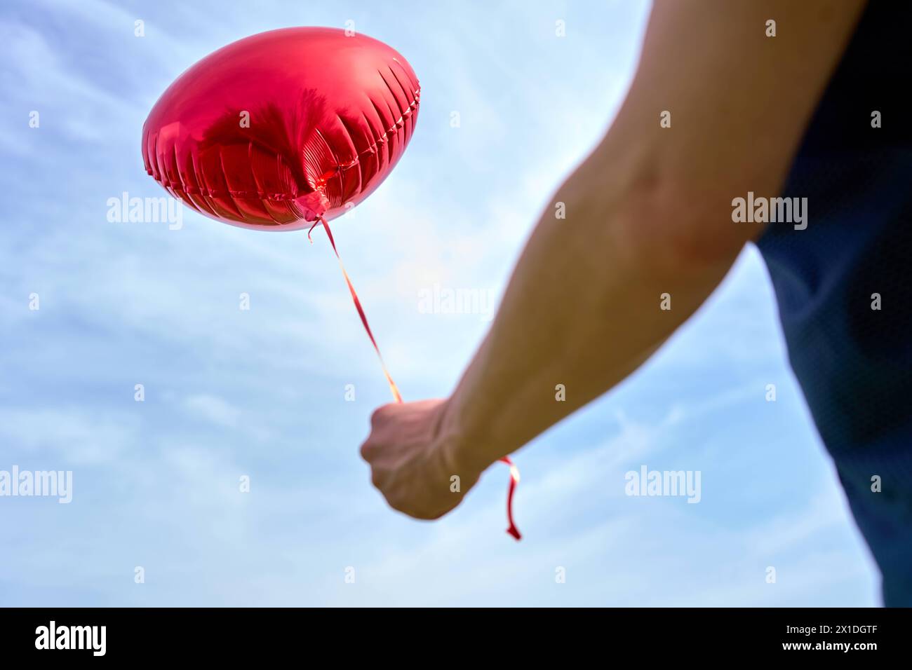 14 April 2024: Young man holding a red helium balloon in the shape of a ...