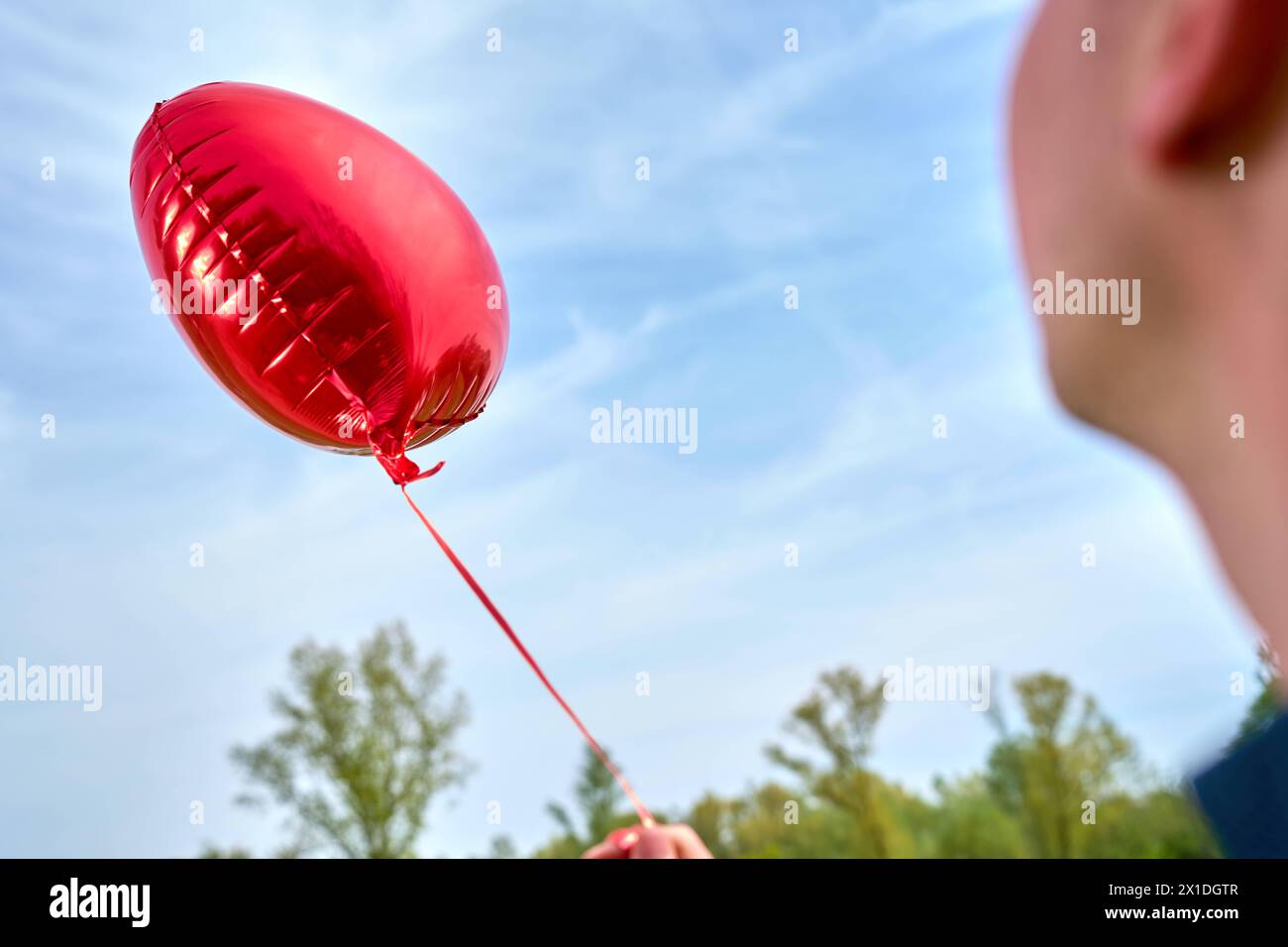 14 April 2024: Young man holding a red helium balloon in the shape of a ...