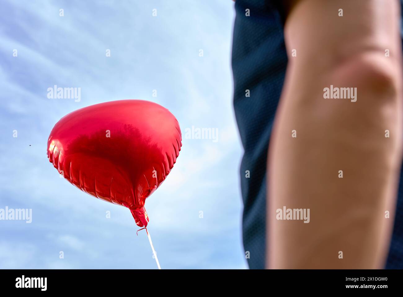 14 April 2024: Young man holding a red helium balloon in the shape of a ...