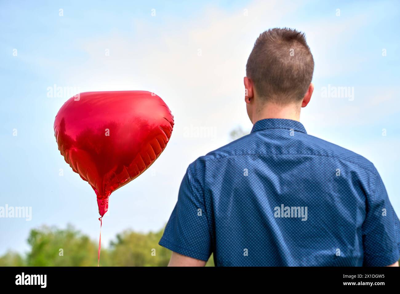 14 April 2024: Young man holding a red helium balloon in the shape of a ...