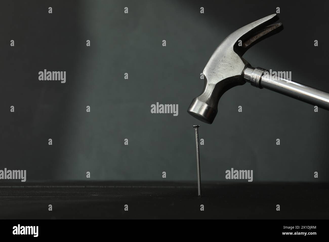 Hammering metal nail on wooden table against black background. Space ...