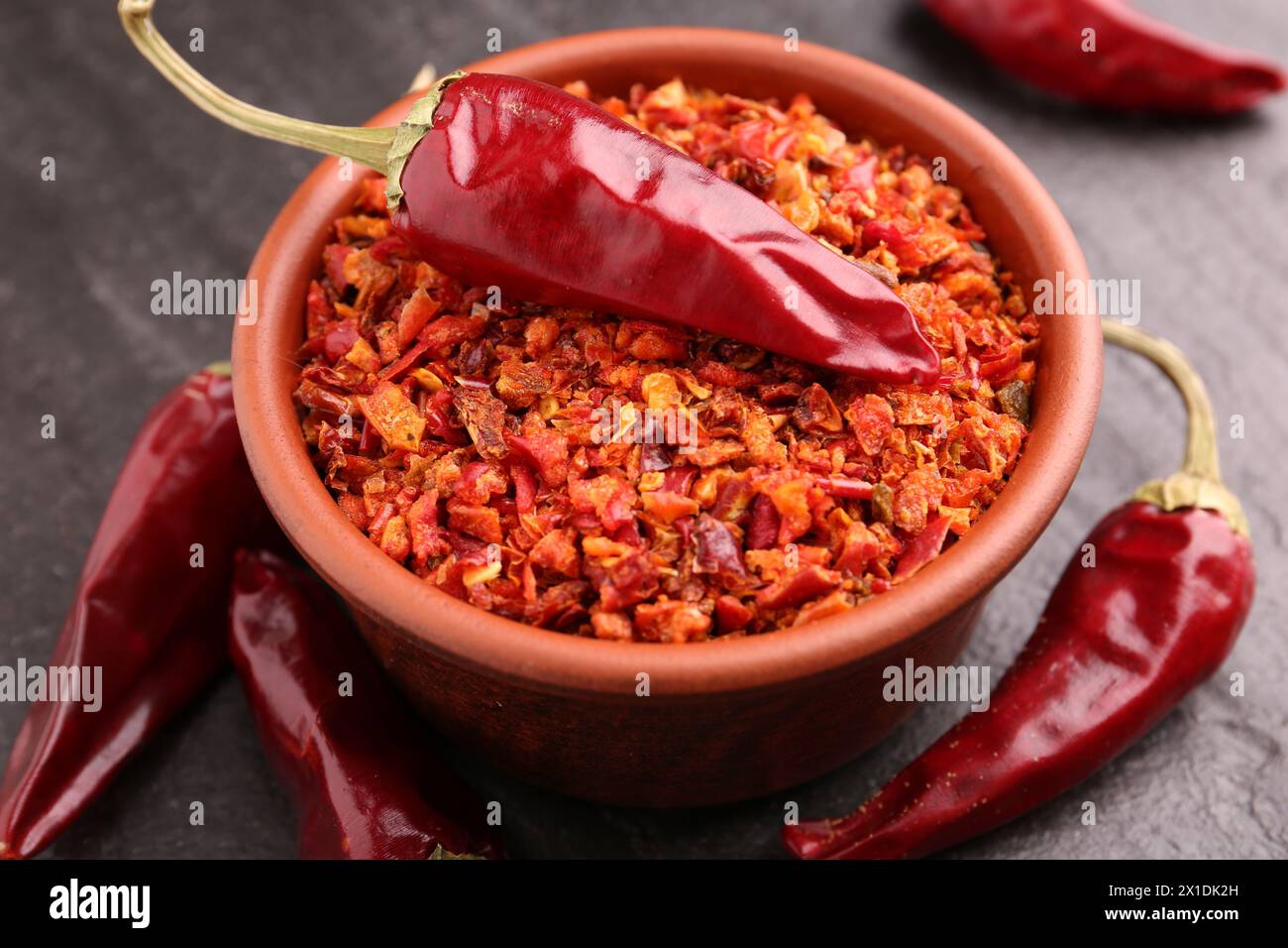 Chili pepper flakes in bowl and pods on dark textured table, closeup ...