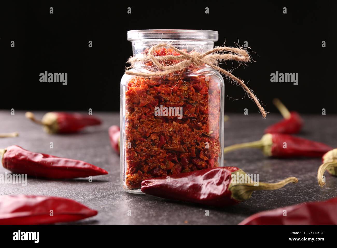 Chili pepper flakes in jar and pods on textured table against black ...