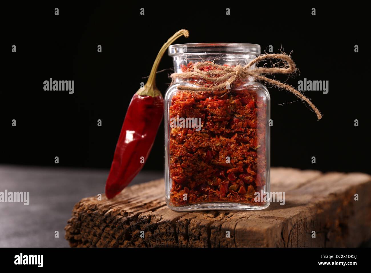 Chili pepper flakes in jar and pod on table against black background ...
