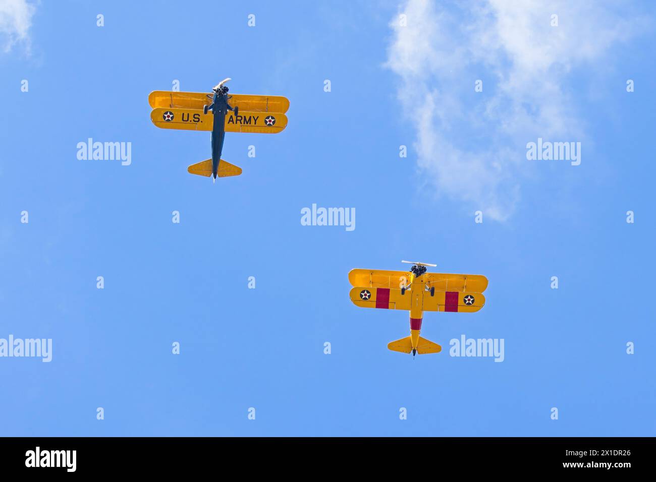 Two old style biplanes fly directly over head in the bright blue sky ...