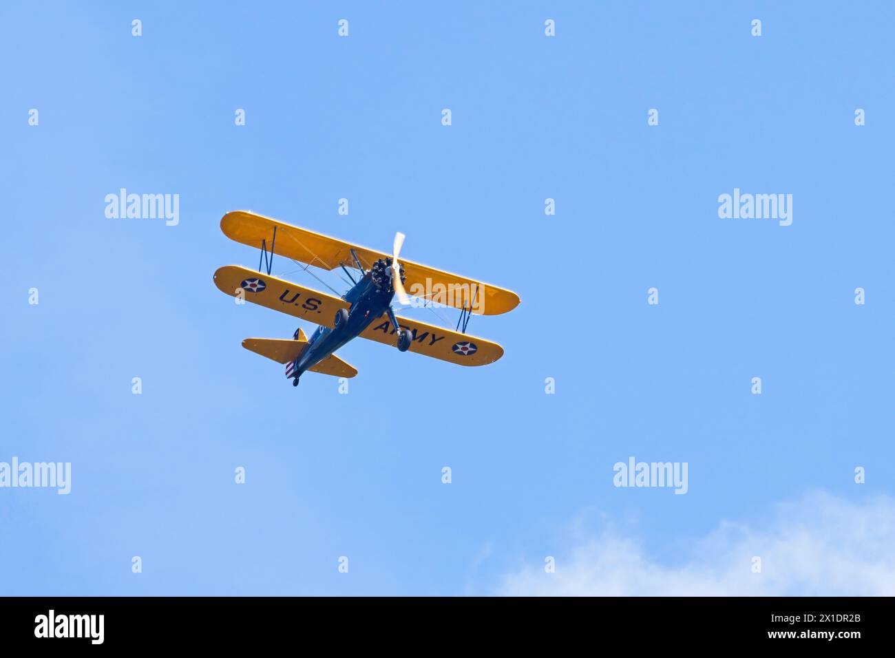 A yellow old style biplane soars up in the bright blue sky near Liberty ...
