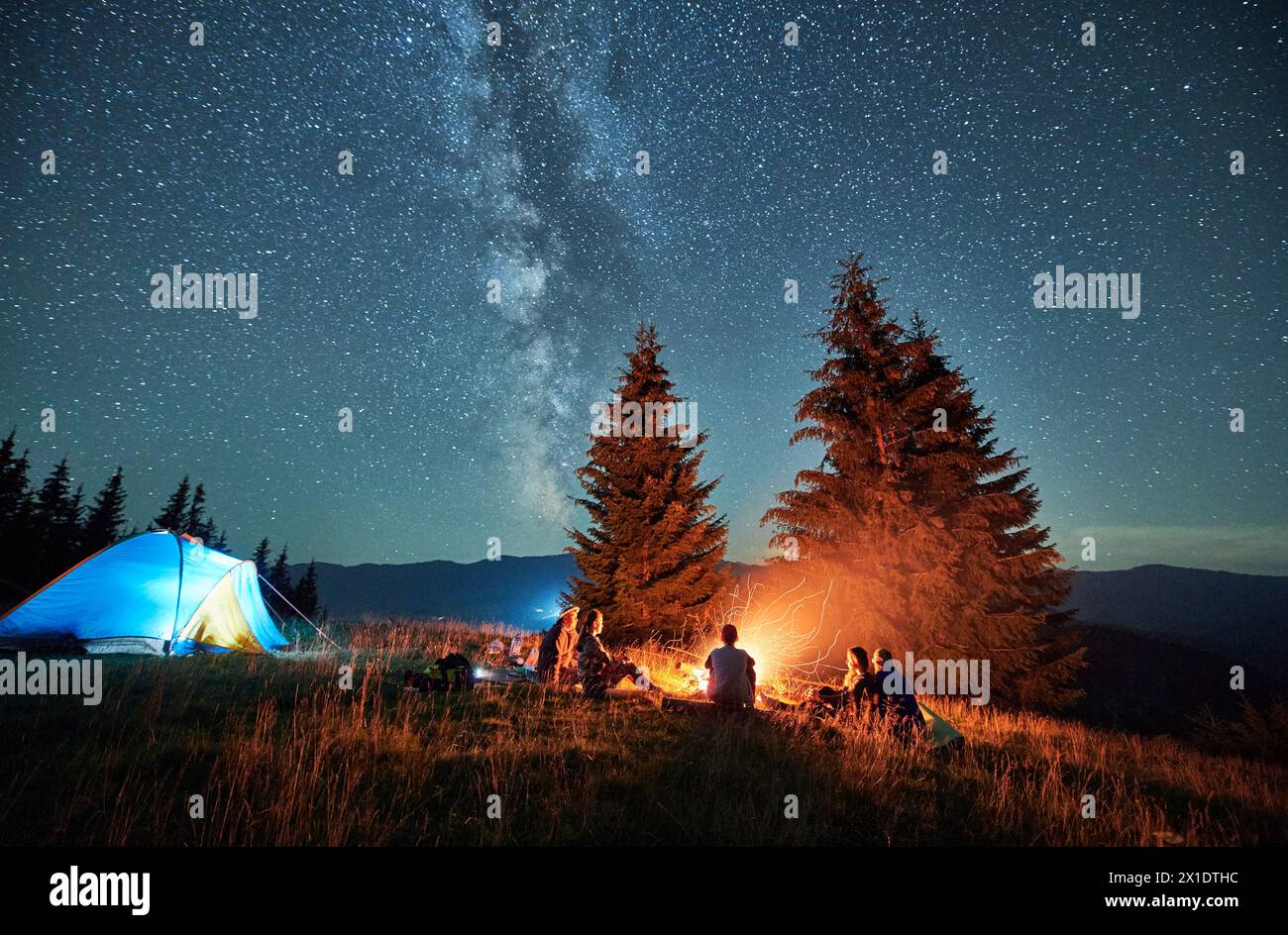 Night camping in mountains under starry sky. Group of people tourists having a rest near ...