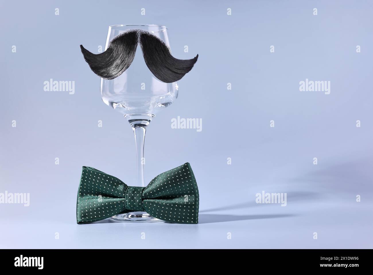 Man's face made of artificial mustache, bow tie and wine glass on light ...