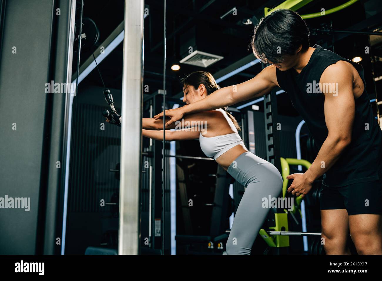 Male fitness coach teaching a woman how to use a pulldown cable machine ...