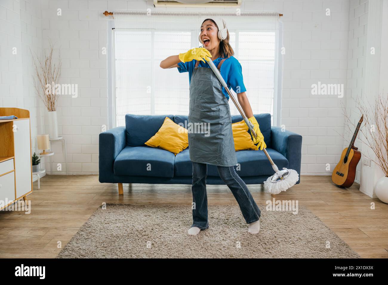 Happy Asian housewife enjoys singing her favorite song using a vacuum ...