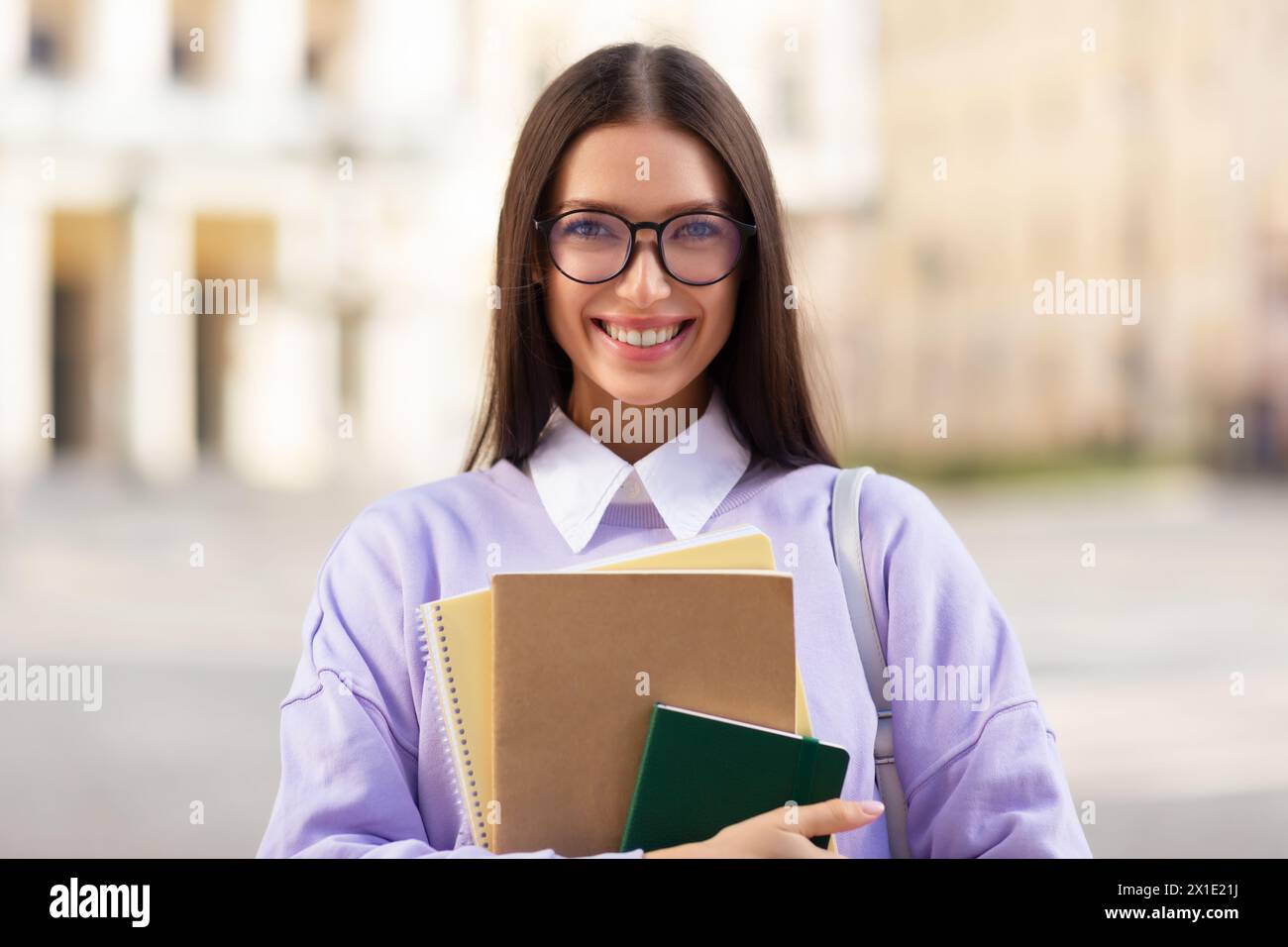 Smiling student holding books in urban setting Stock Photo - Alamy