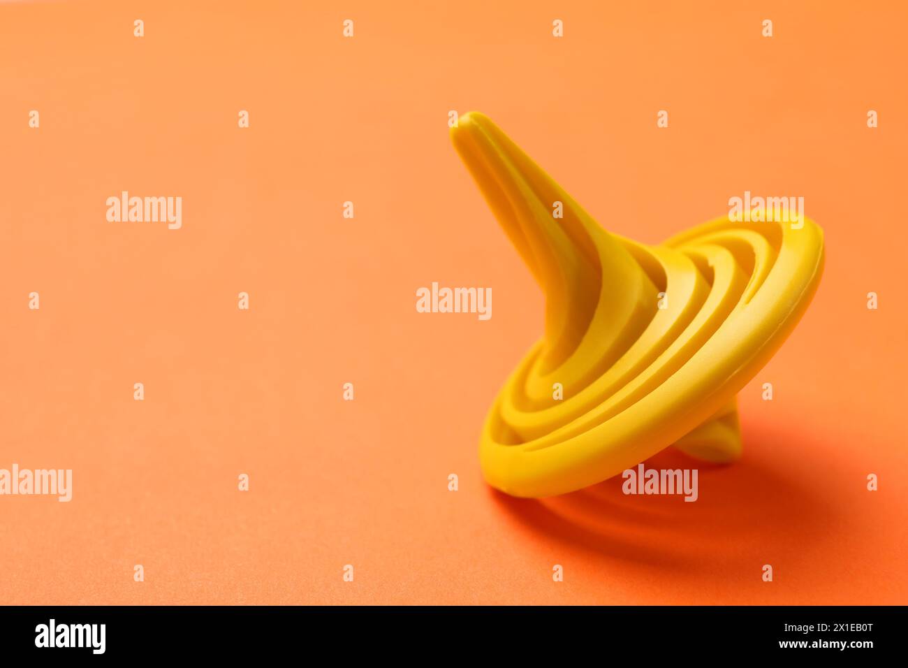 One yellow spinning top on orange background, closeup. Space for text ...