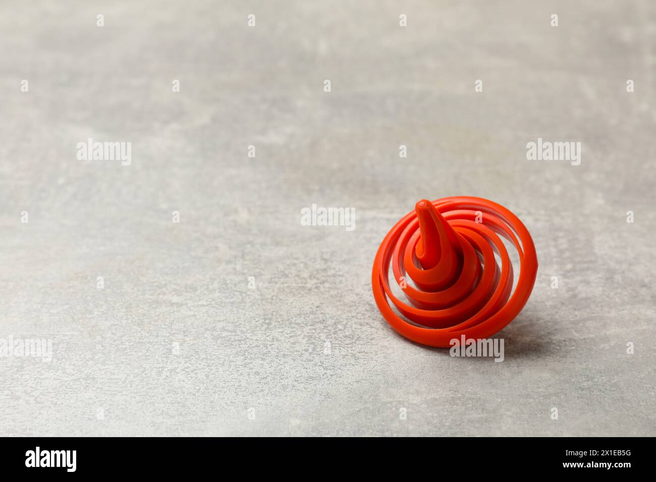 Red spinning top on grey textured background, closeup. Space for text ...