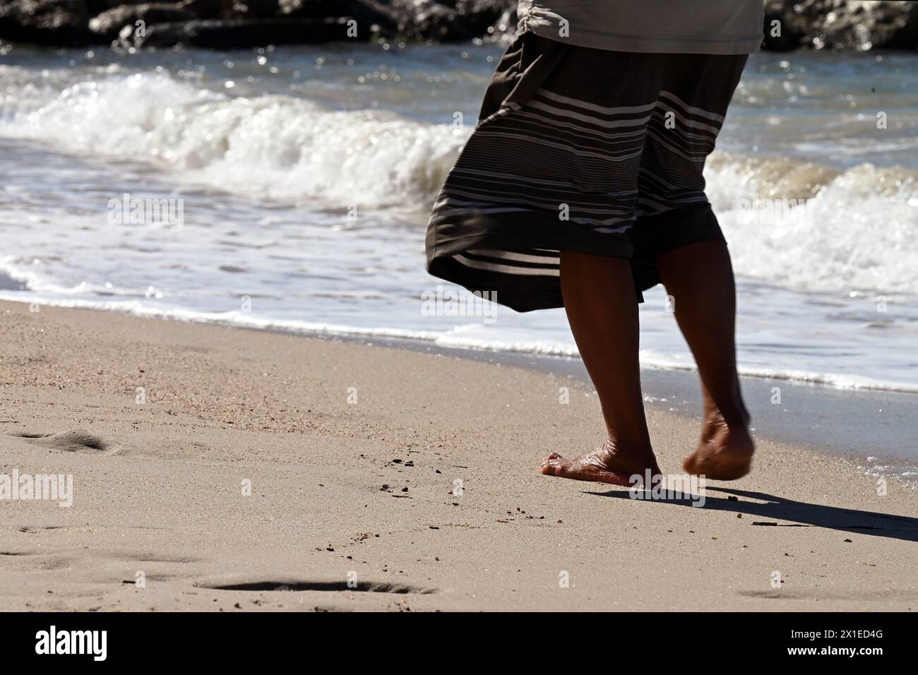Bottom half of woman in a dress from behind walking barefoot on a sandy ...