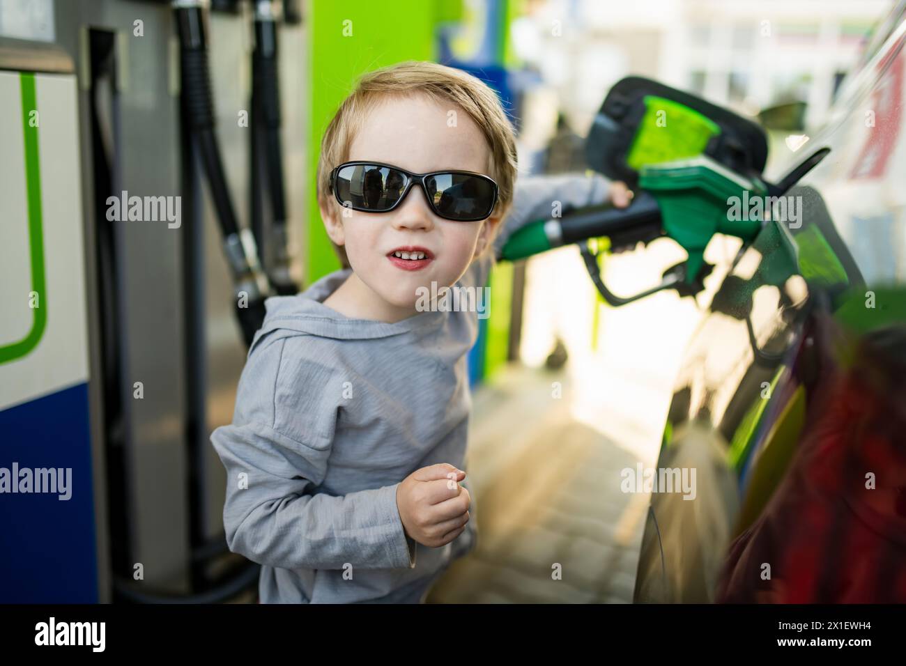 Cute little blond boy holding pump nozzle. Small funny kid helping ...