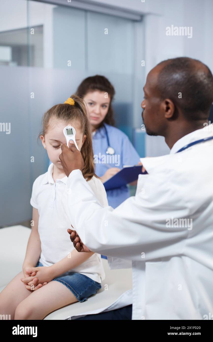 African American physician using thermometer on little girl to check ...