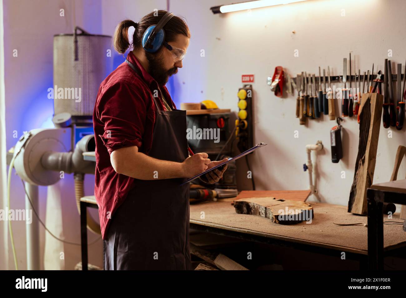 Carpenter wearing safety glasses drawing blueprints on notepad to make creative wood art pieces ...