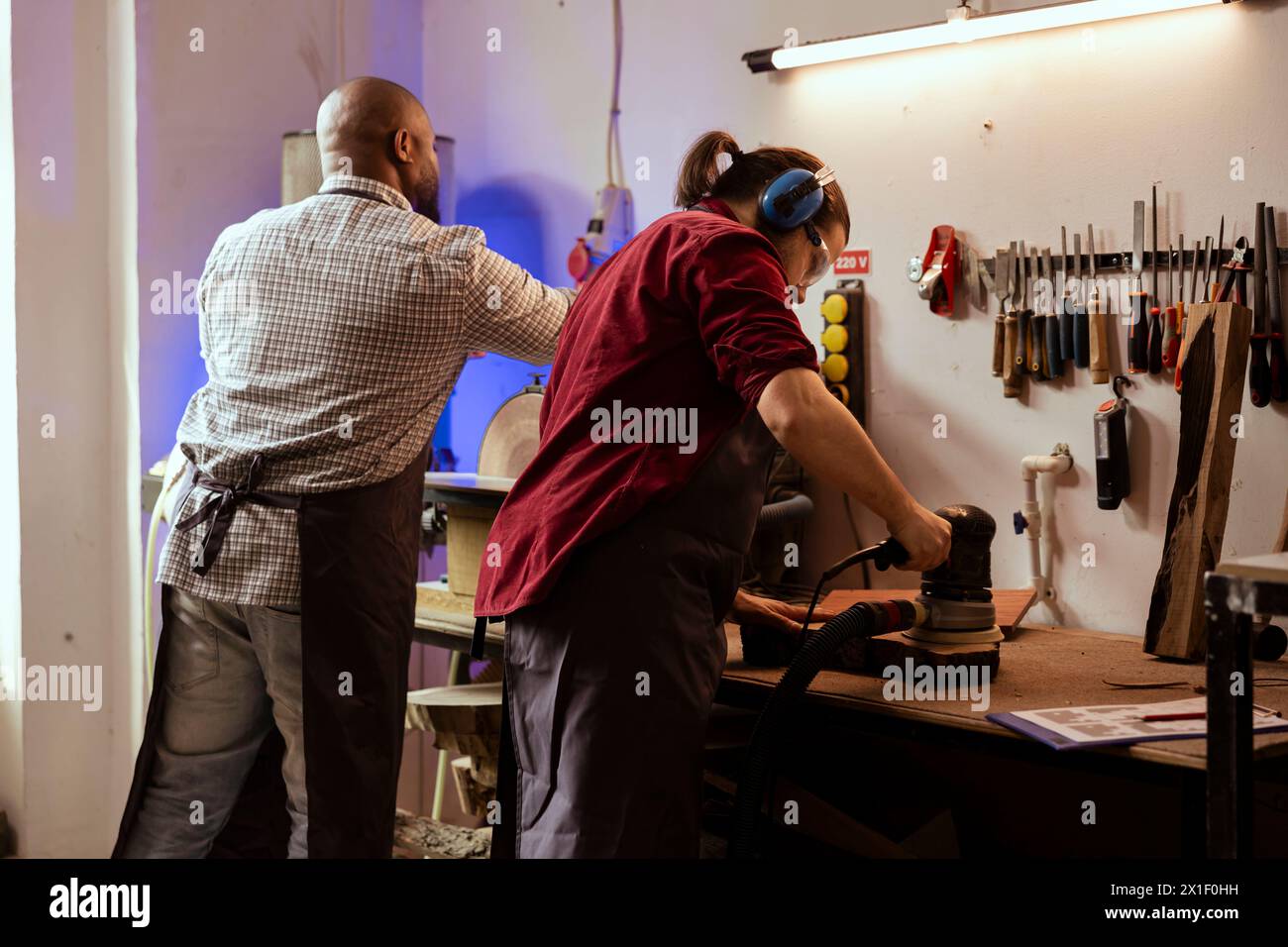 Master carpenter and apprentice using orbital sander on lumber ...