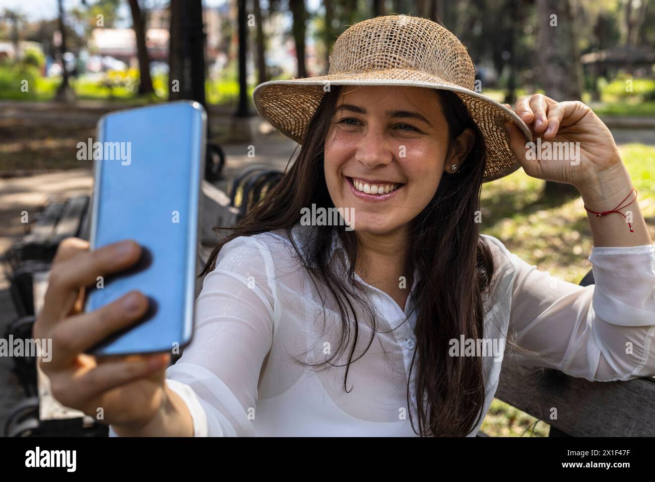 In spring young Latin American woman (33) is sitting on a park bench ...