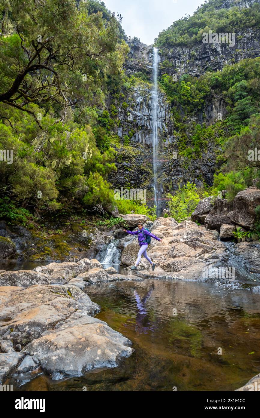 Description: Female tourist with backpack jumps over rocks at waterfall ...