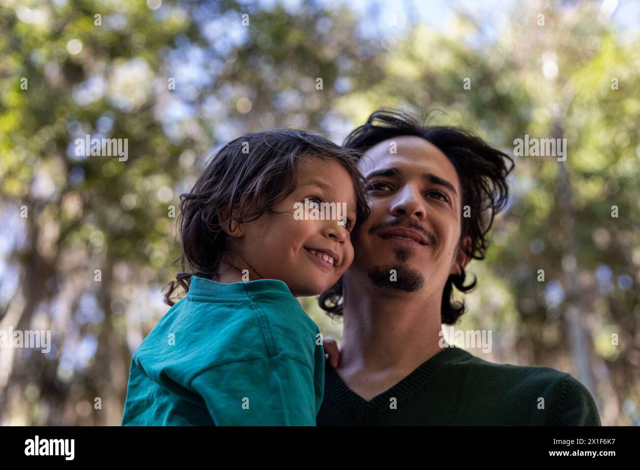 Latin American dad carries his 3 year old son in his arms in the park ...