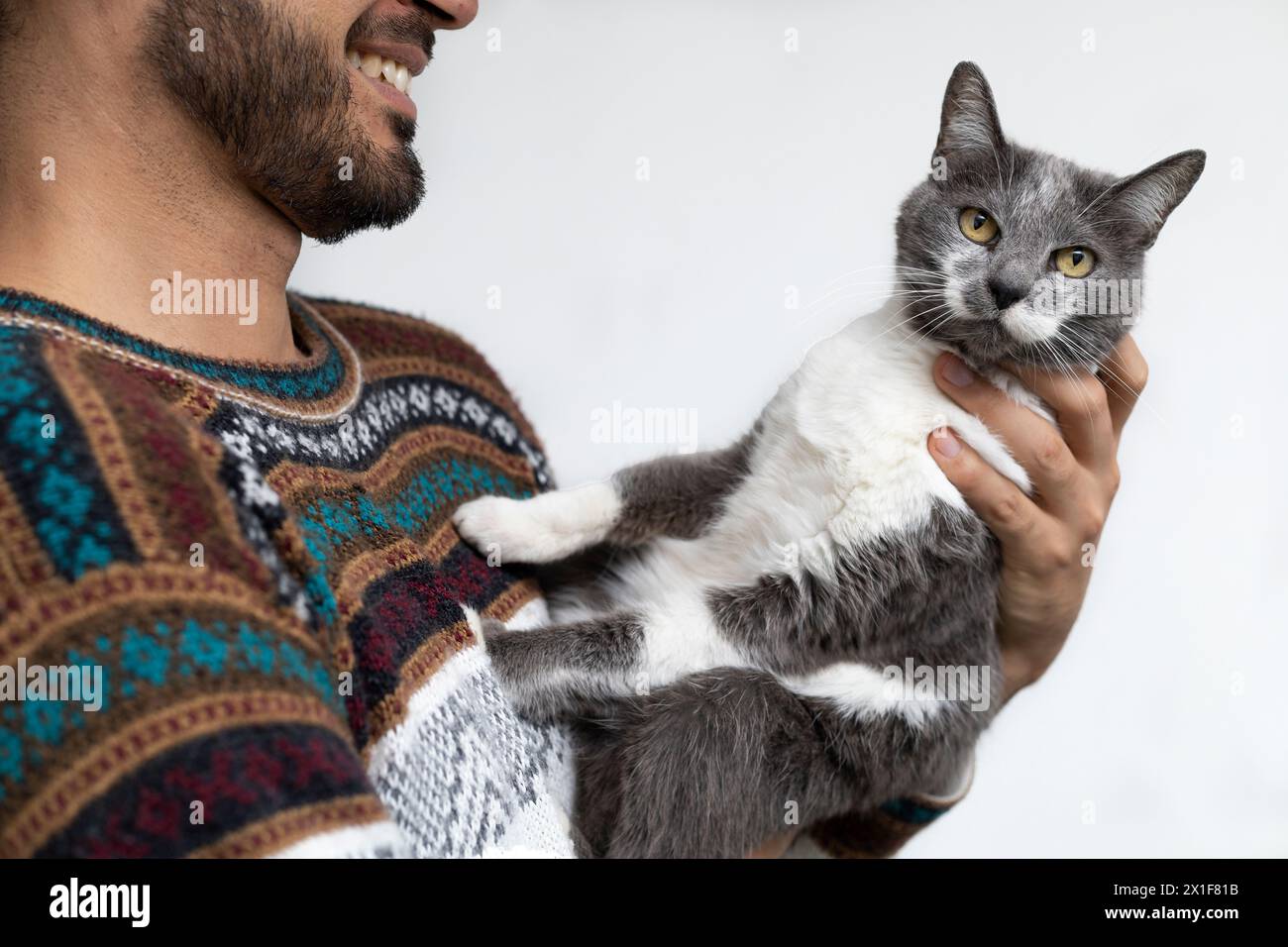 Latin American man smiles while holding his cat affectionately in his ...