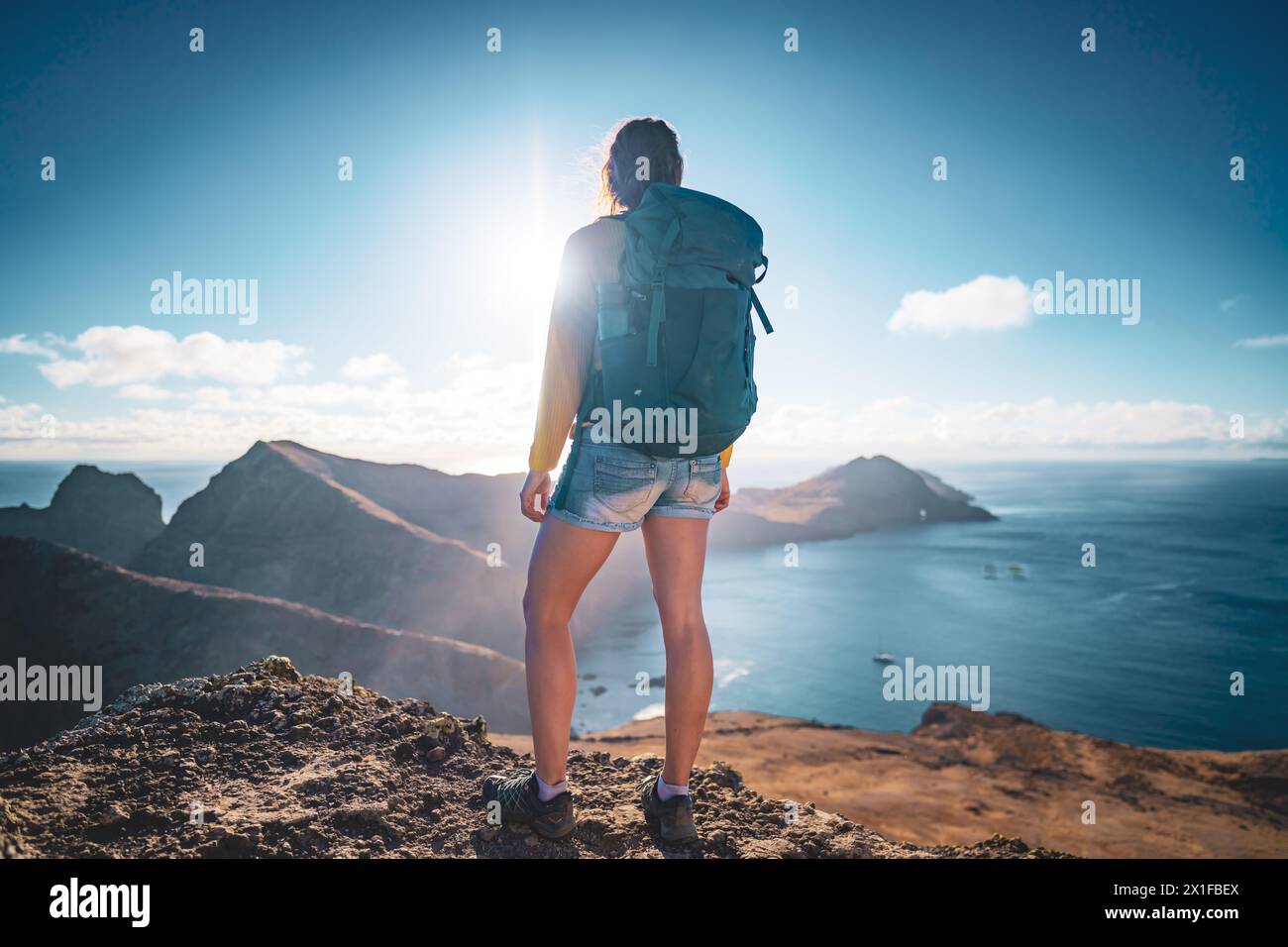 Description: Low angle back view of a female backpacker standing on top ...
